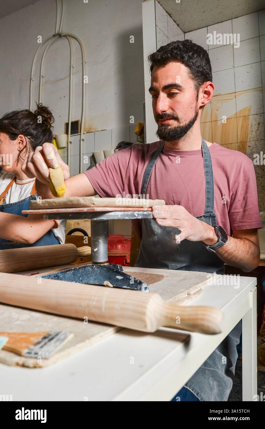 Craftsman smoothing a clay slab in a pottery workshop, using a sponge ...