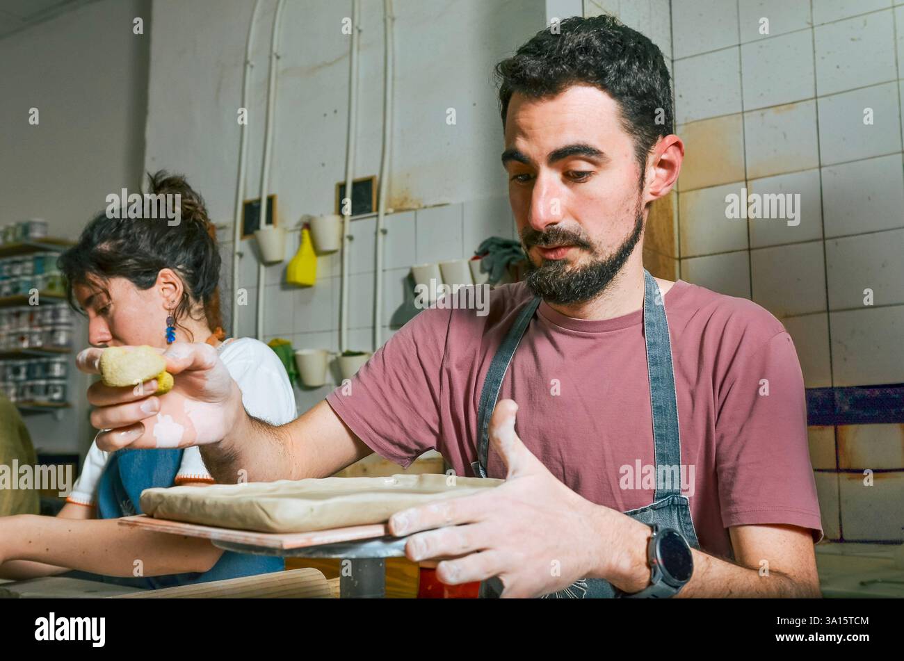 Craftsman shaping clay on a slab roller in pottery studio, working with ...