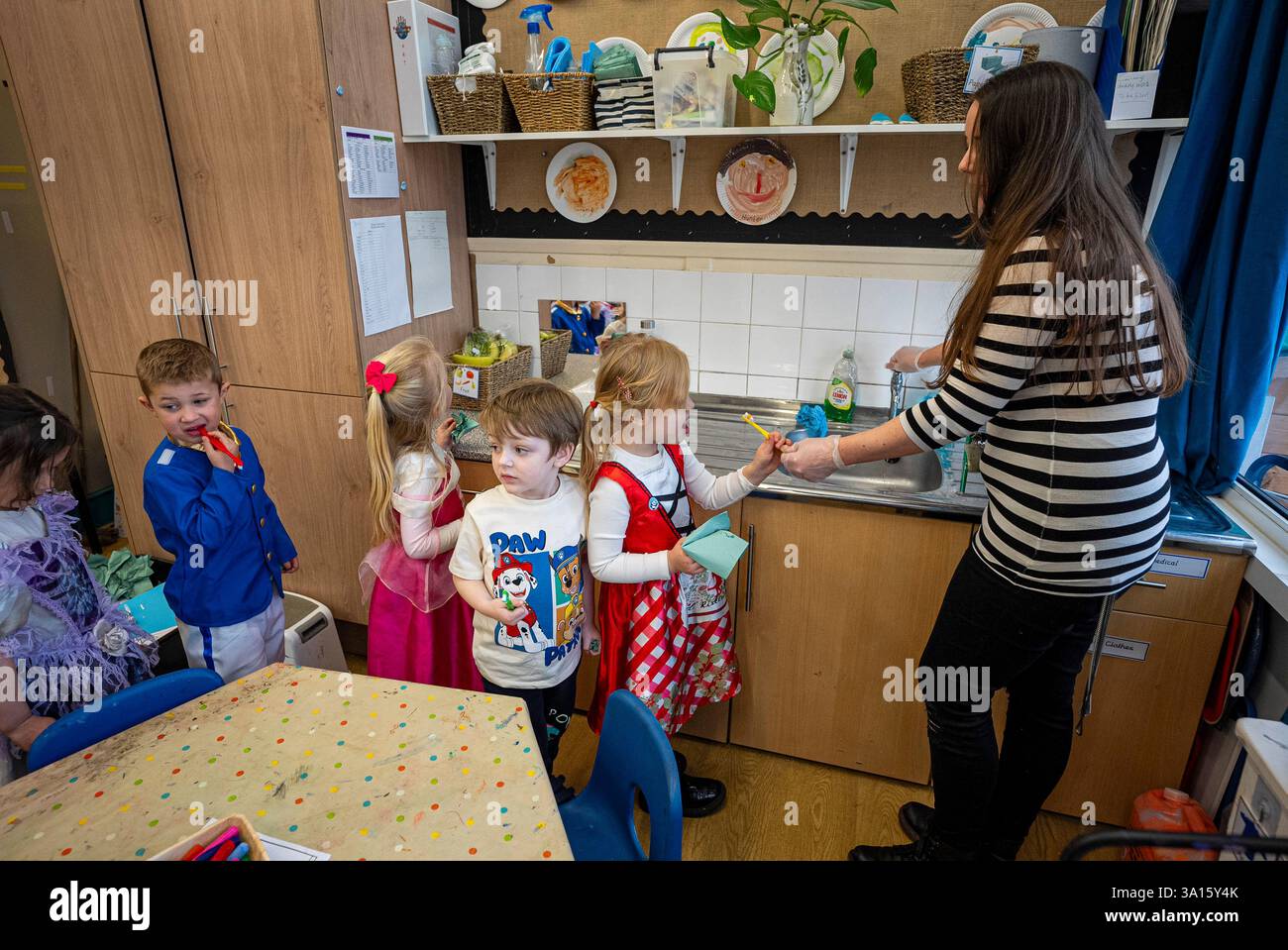 School children are helped to rinse their toothbrushes by a teacher ...