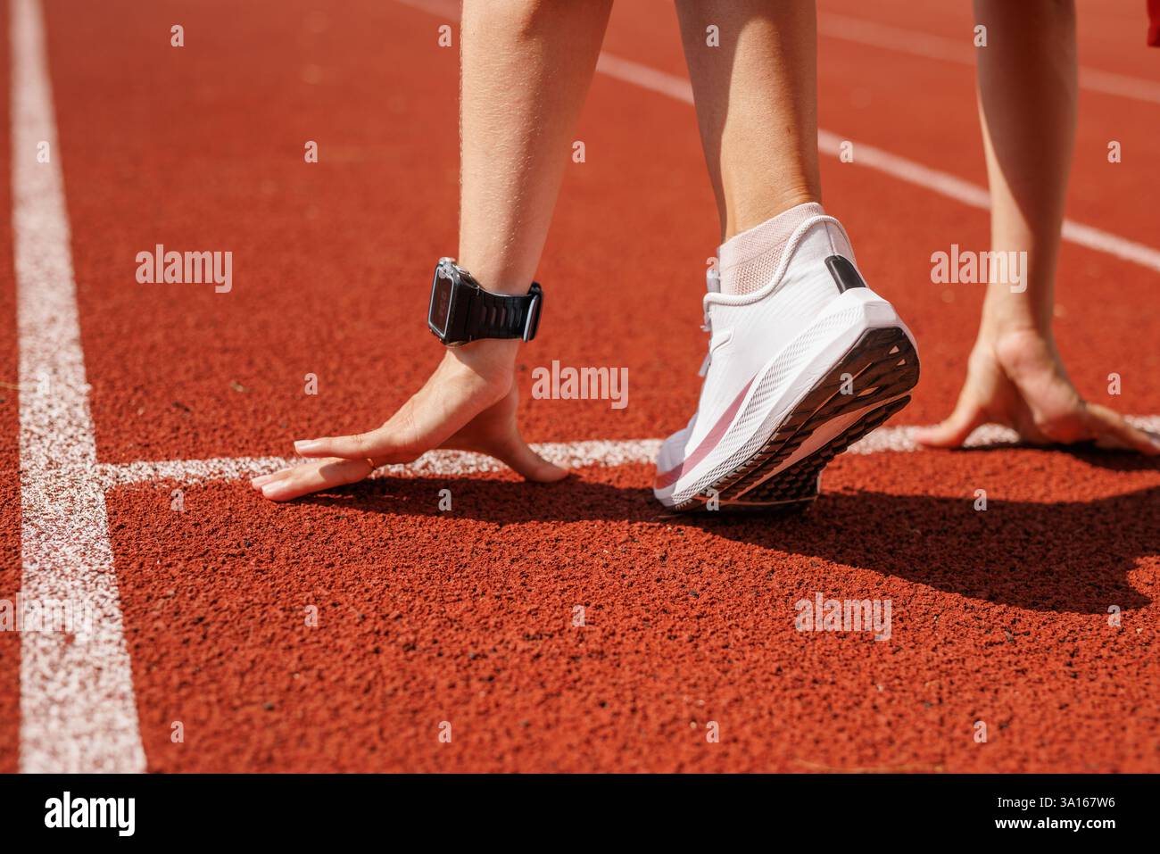 Female athlete at the starting line on a running track, preparing for a ...