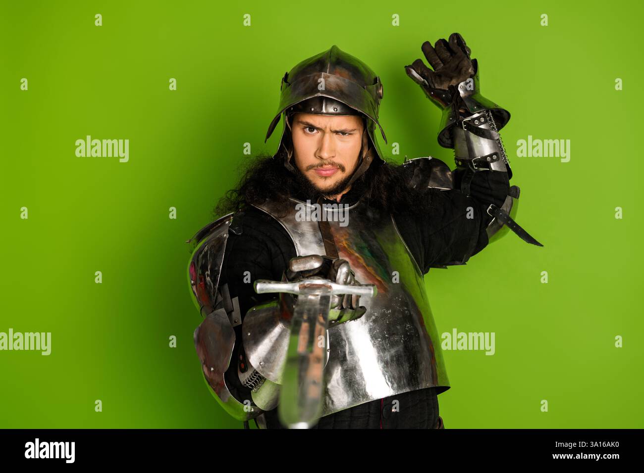 Knight in polished armor holding a sword posing against a vibrant green ...