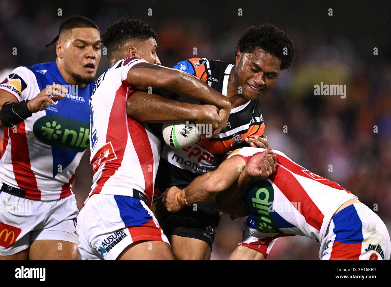 Sione Fainu of the Tigers is tackled by Kai Pearce-Paul (left) and ...
