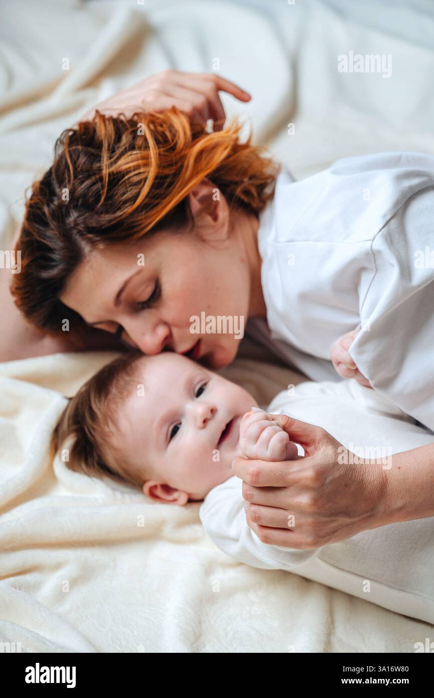 A loving mother and her newborn baby lie on the floor, embracing and ...