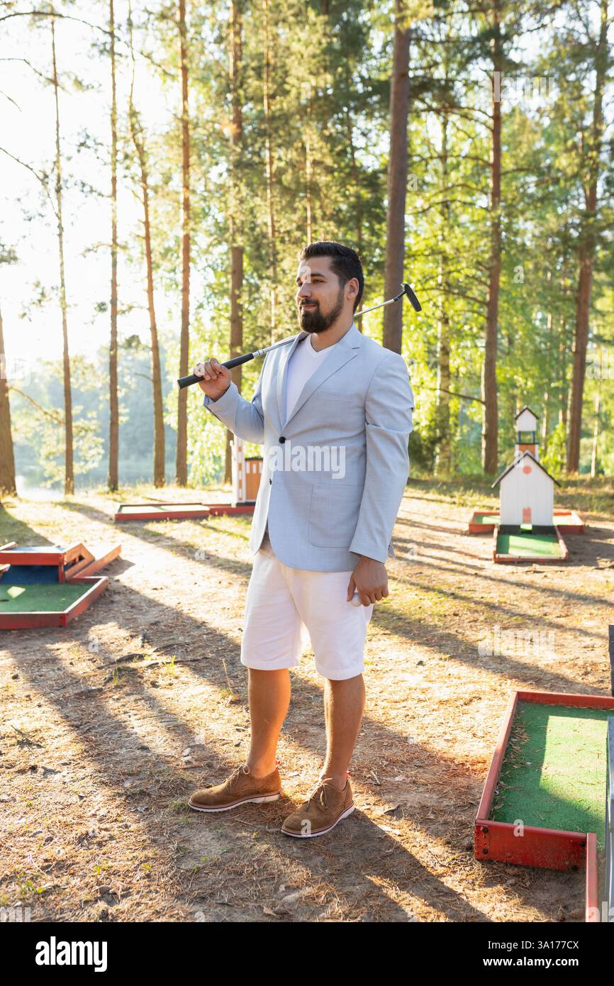 Portrait of young adult mini golf player with club on court in forest ...