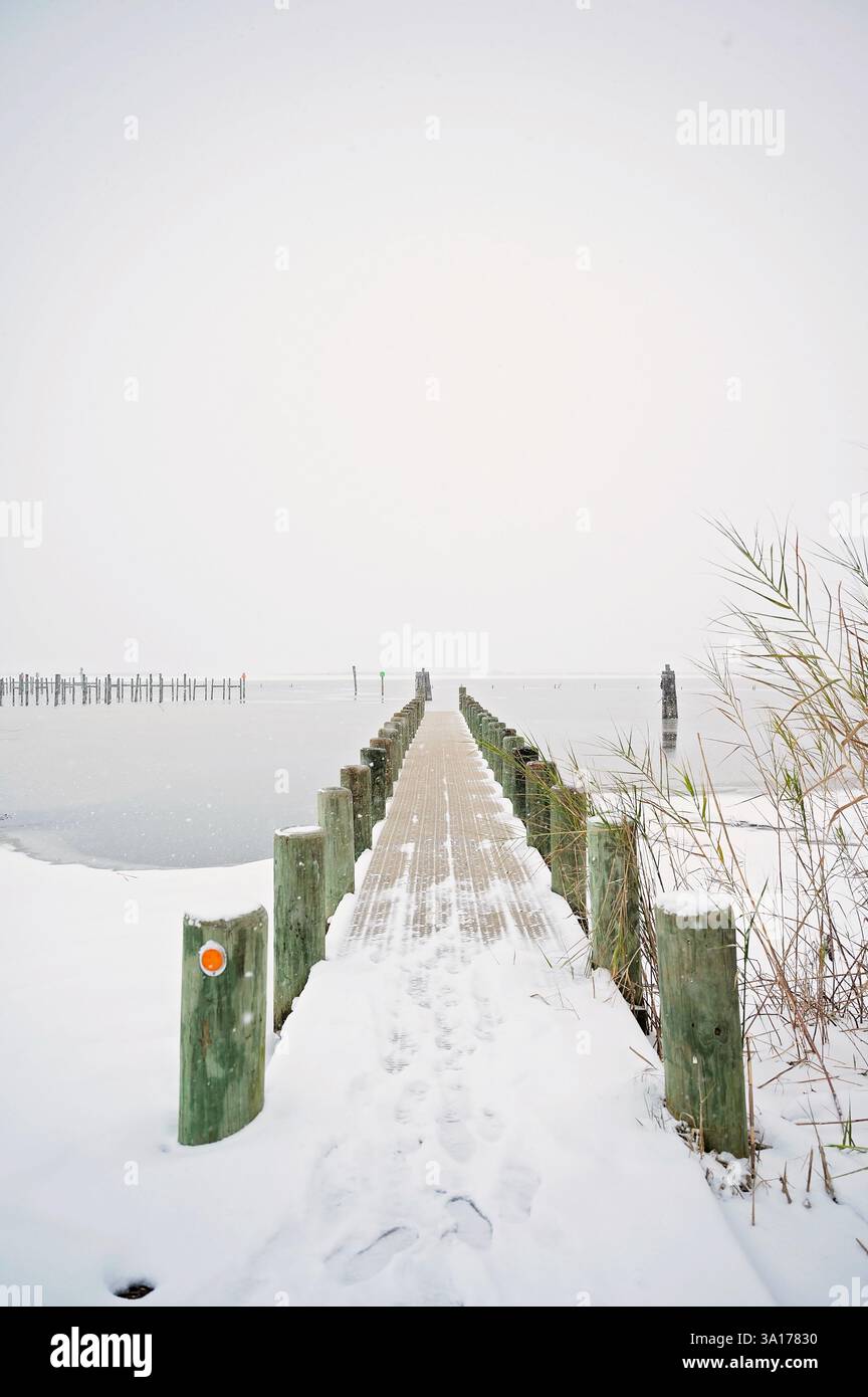 Snow-covered dock leading into a frozen waterfront with footprints ...