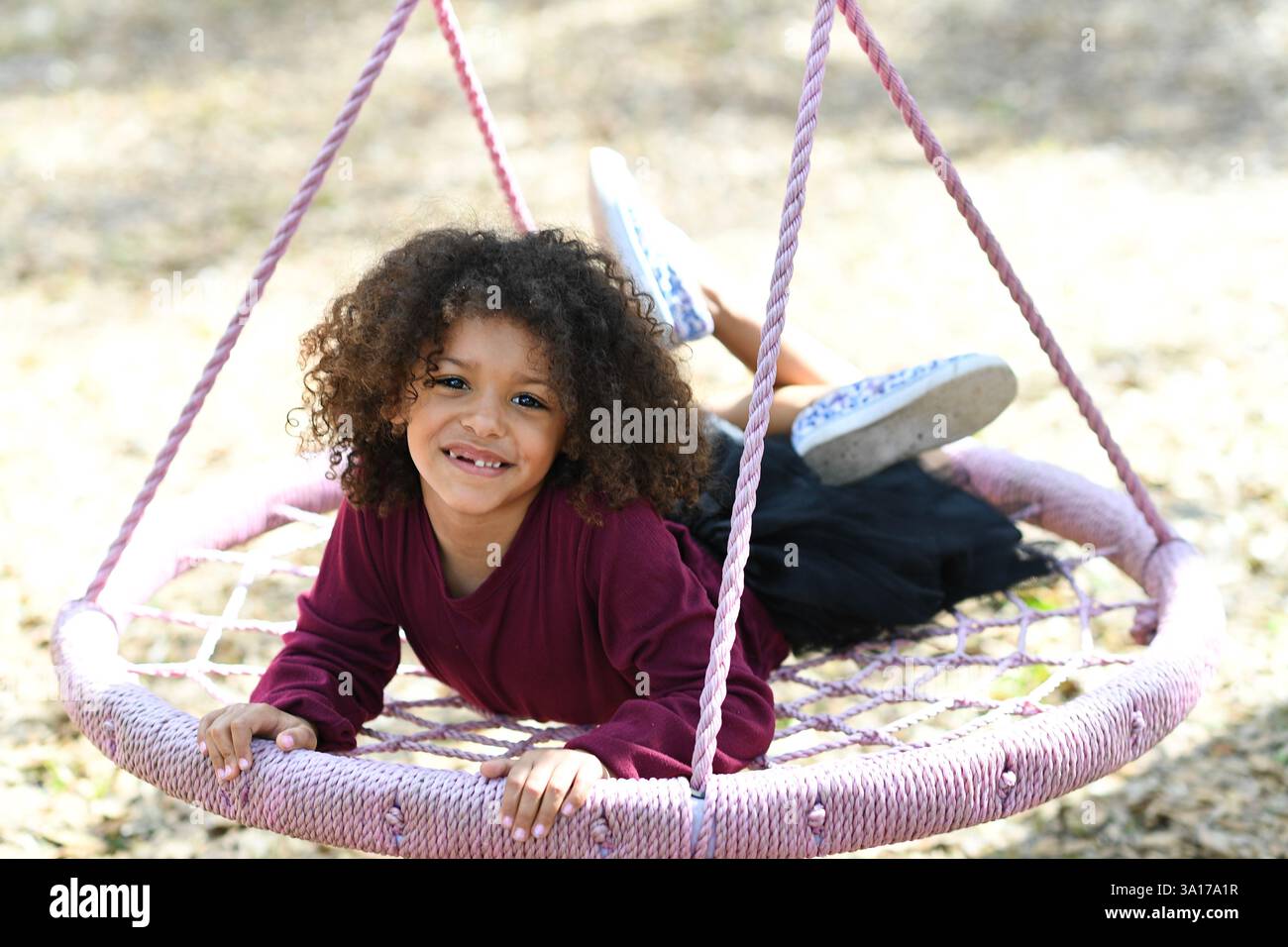 Smiling girl lounging on a pink rope swing, enjoying outdoor pla Stock ...
