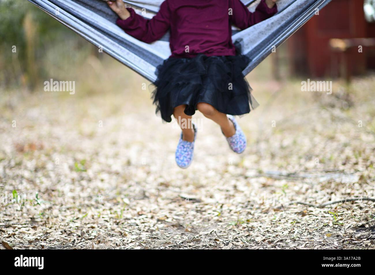 Child swinging in a hammock, legs dangling playfully above groun Stock ...