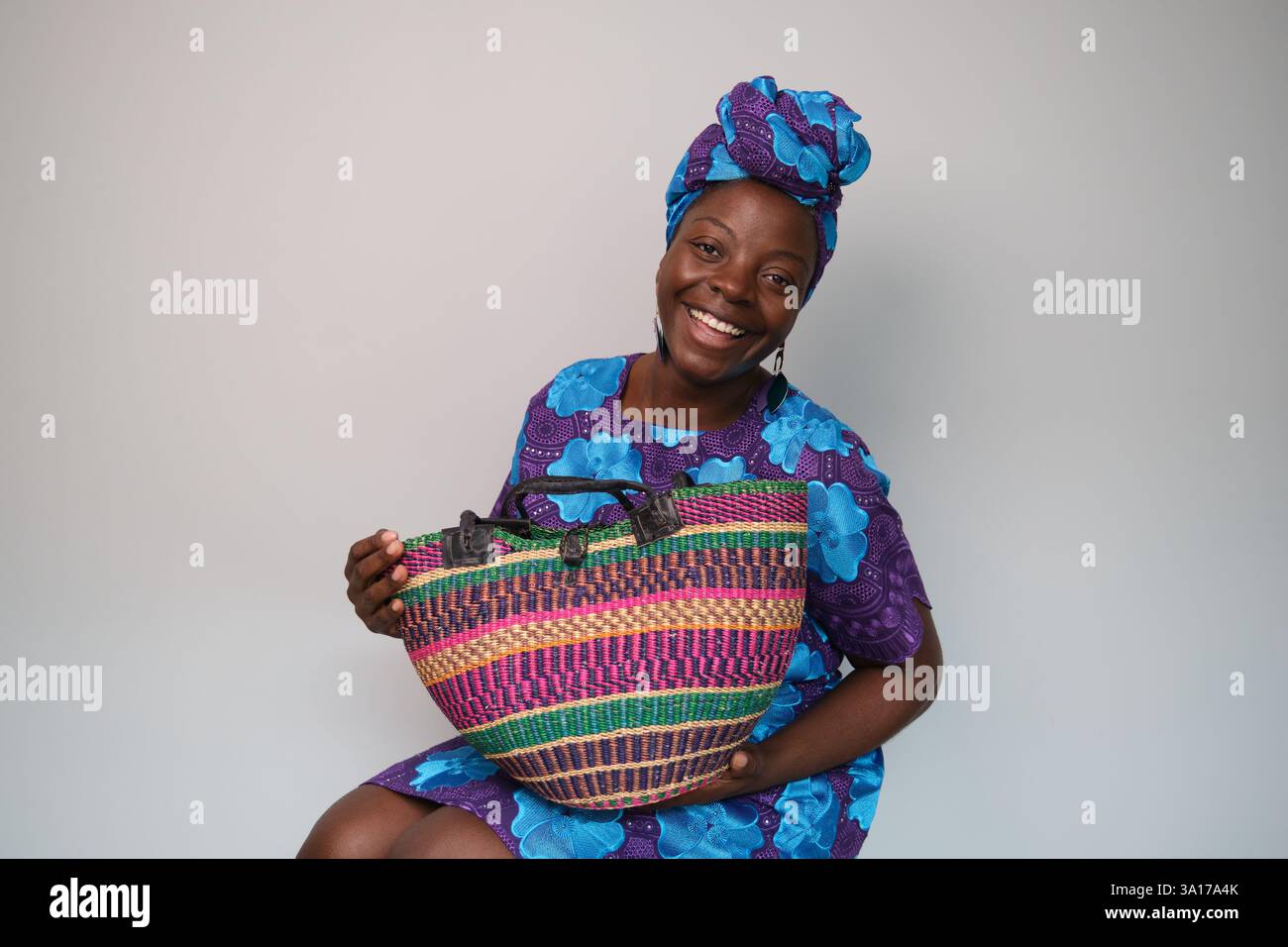 Smiling african woman holding colorful handmade bag sitting on stool ...