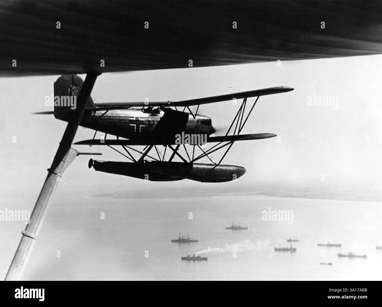 Heinkel He 60 seaplane flying over a convoy of ships, possibly off ...