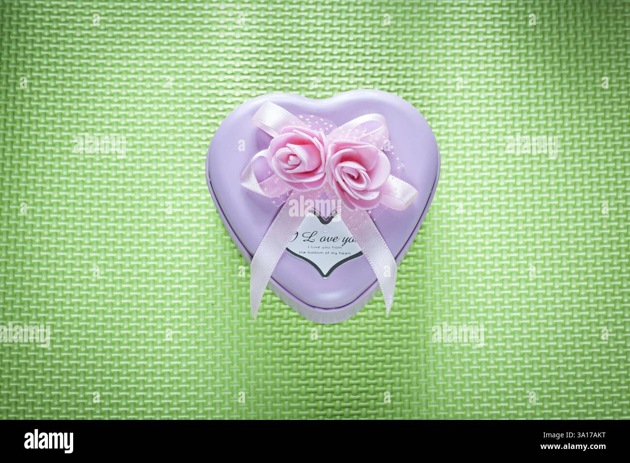 Metal purple heart-shaped present box with bow on green background ...