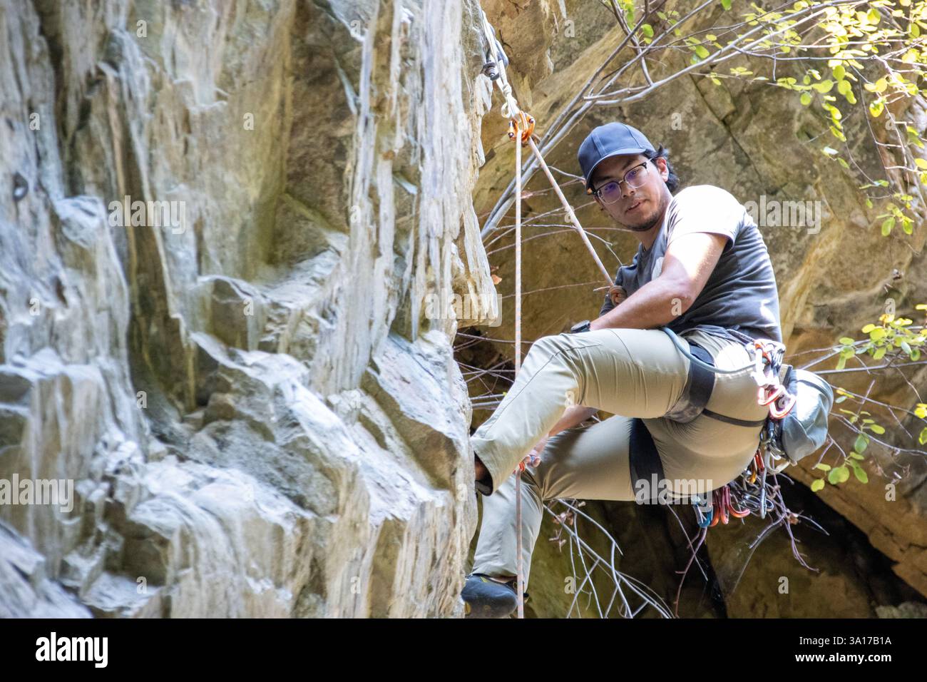 A rock climber sits in climbing gear and looks down cliff Stock Photo ...