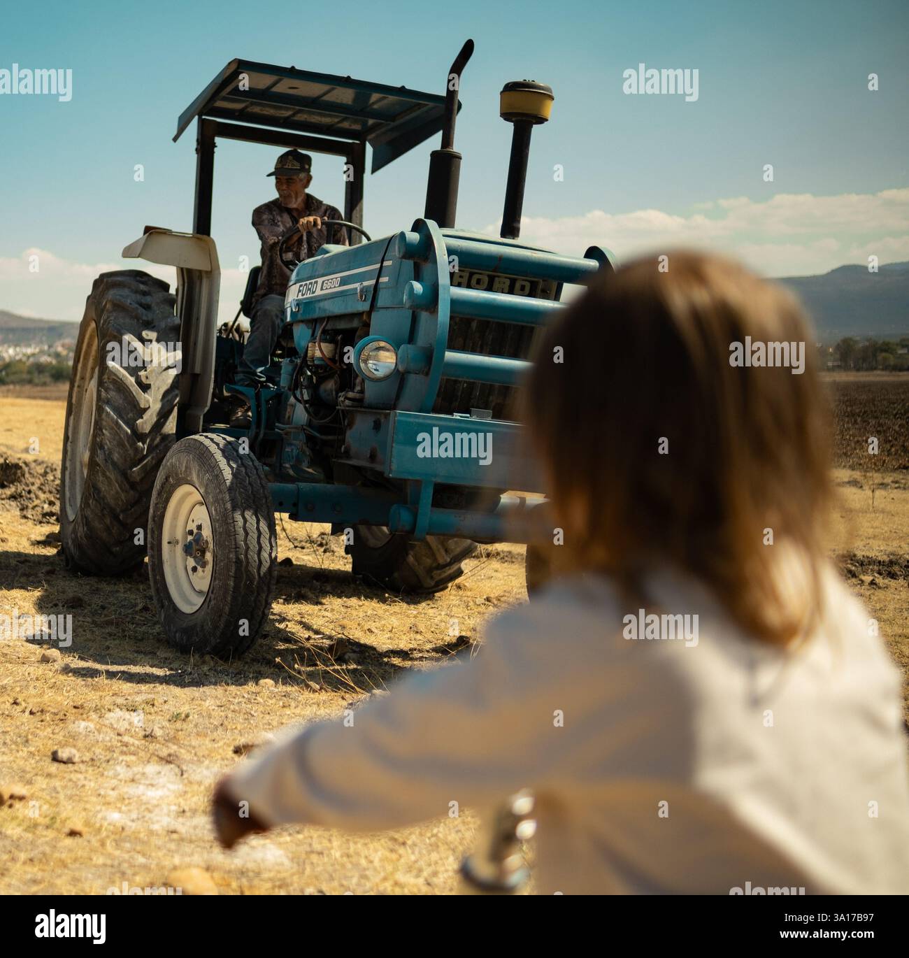 kid on bike watching man drive tractor Stock Photo - Alamy