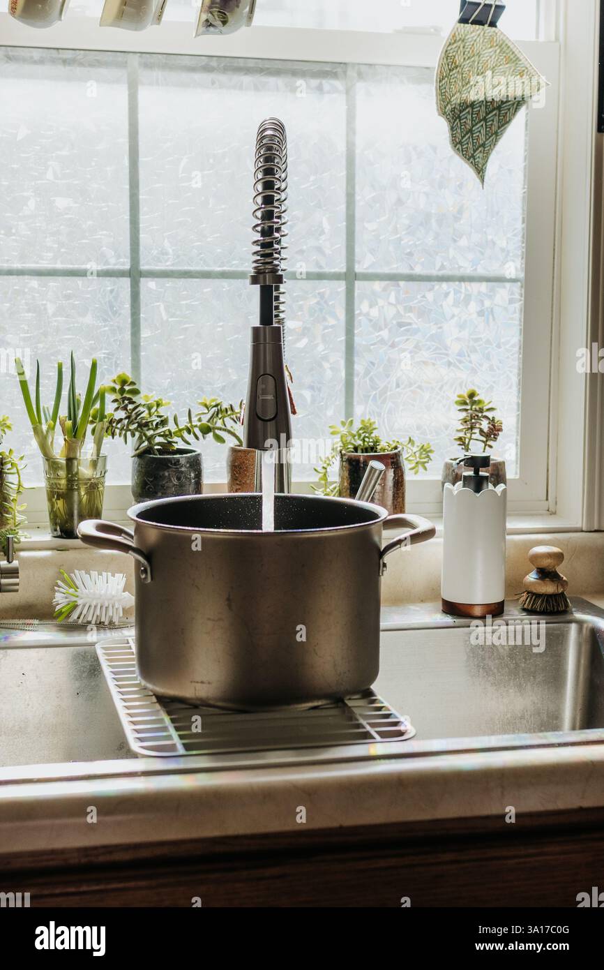 Water runs as soup pot is fill in kitchen sink near window Stock Photo ...