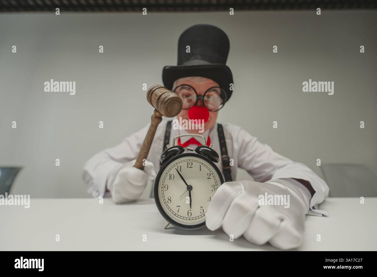 An elderly man dressed as a clown smashes an alarm clock with a hammer ...
