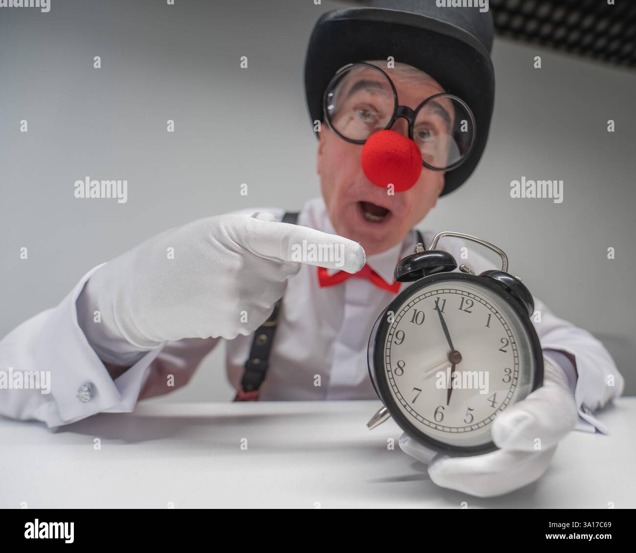 An elderly man in a clown costume points at an alarm clock Stock Photo ...