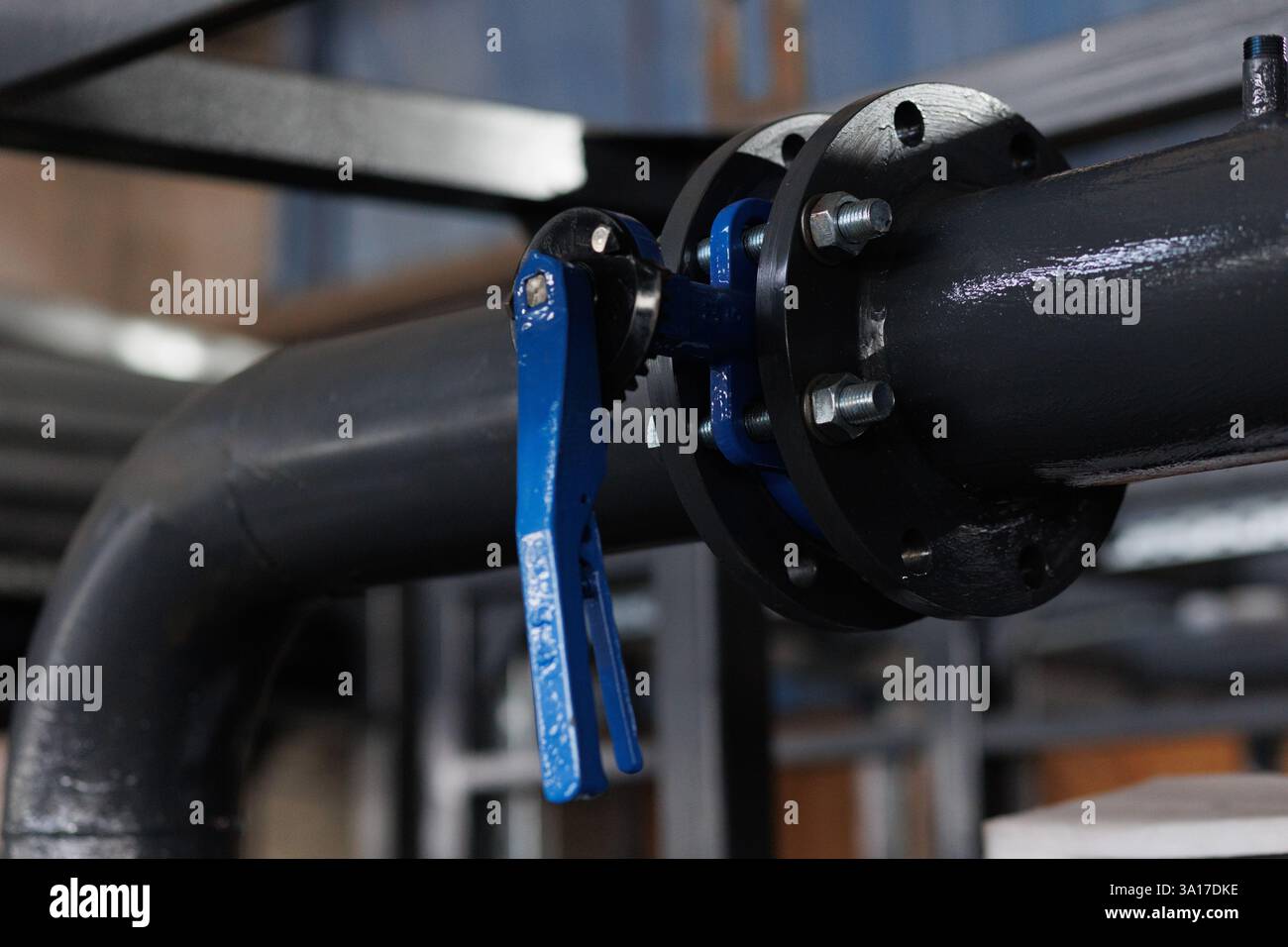A blue valve lever is positioned on a metal pipe, showcasing industrial ...