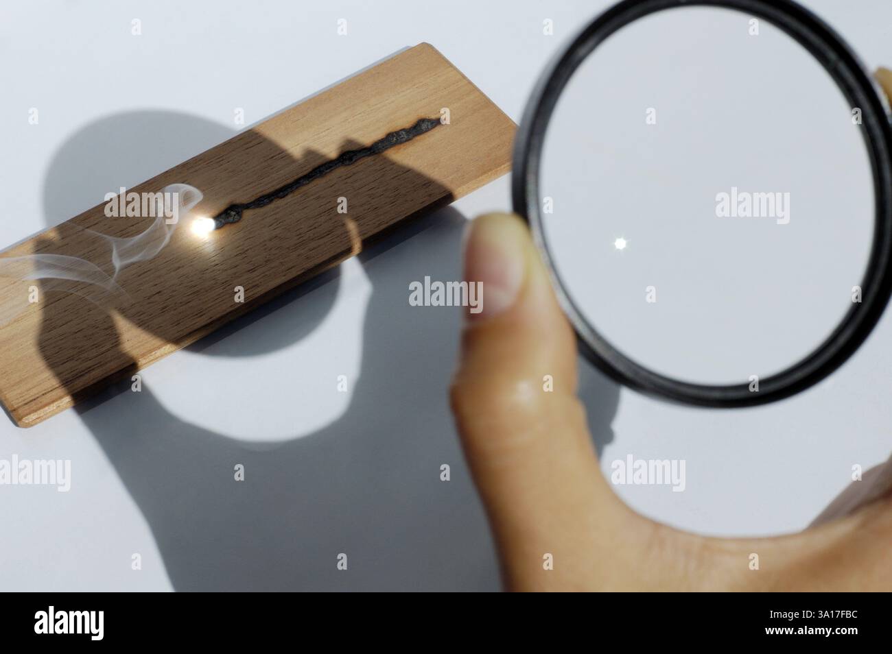 Magnifying glass focused on piece of wood starting fire Stock Photo - Alamy