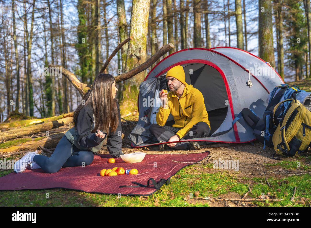 Couple of hikers having a snack next to their tent during a camping ...