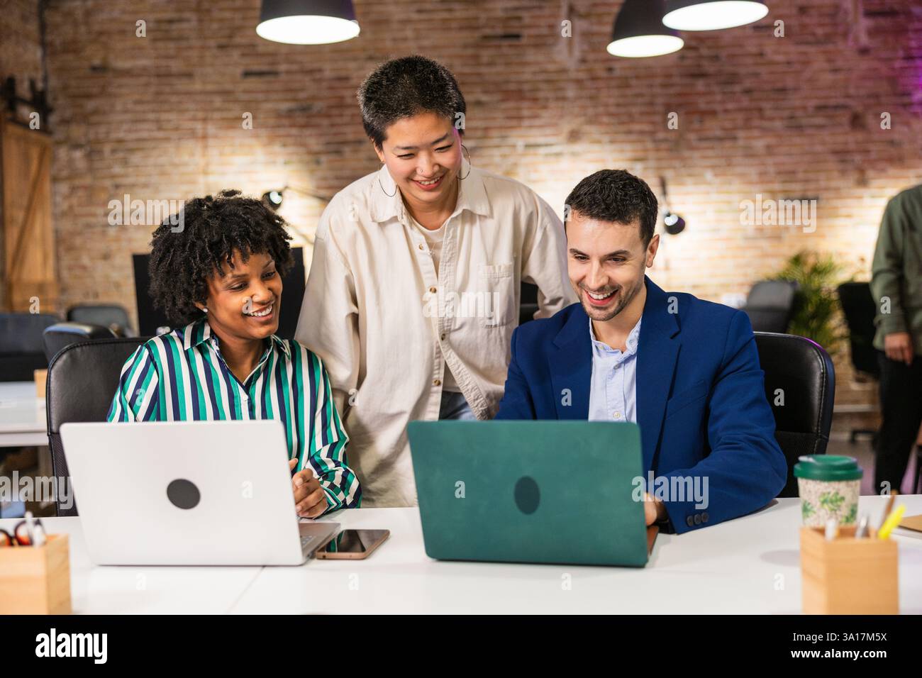 Multi ethnic team collaborating on laptops in modern office Stock Photo - Alamy
