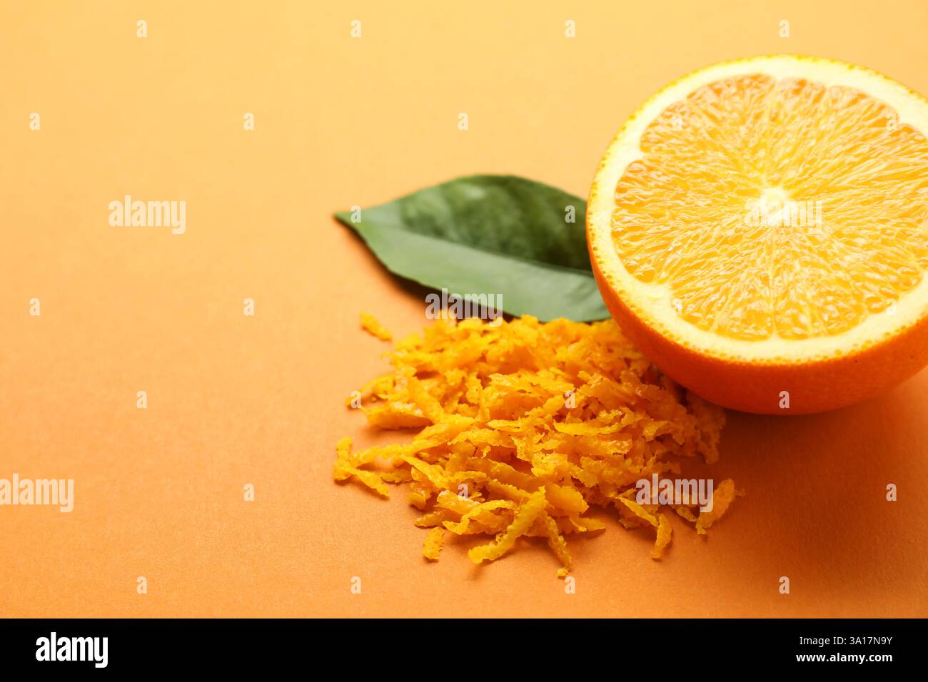 Pile of fresh orange zest, cut fruit and leaf on color background ...