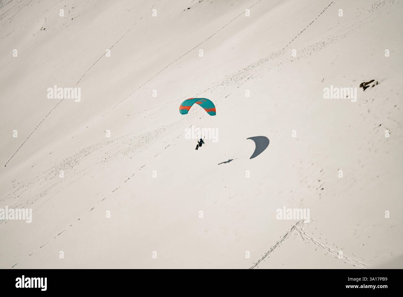 Paraglider soaring through the clouds above a snowy mountain range ...