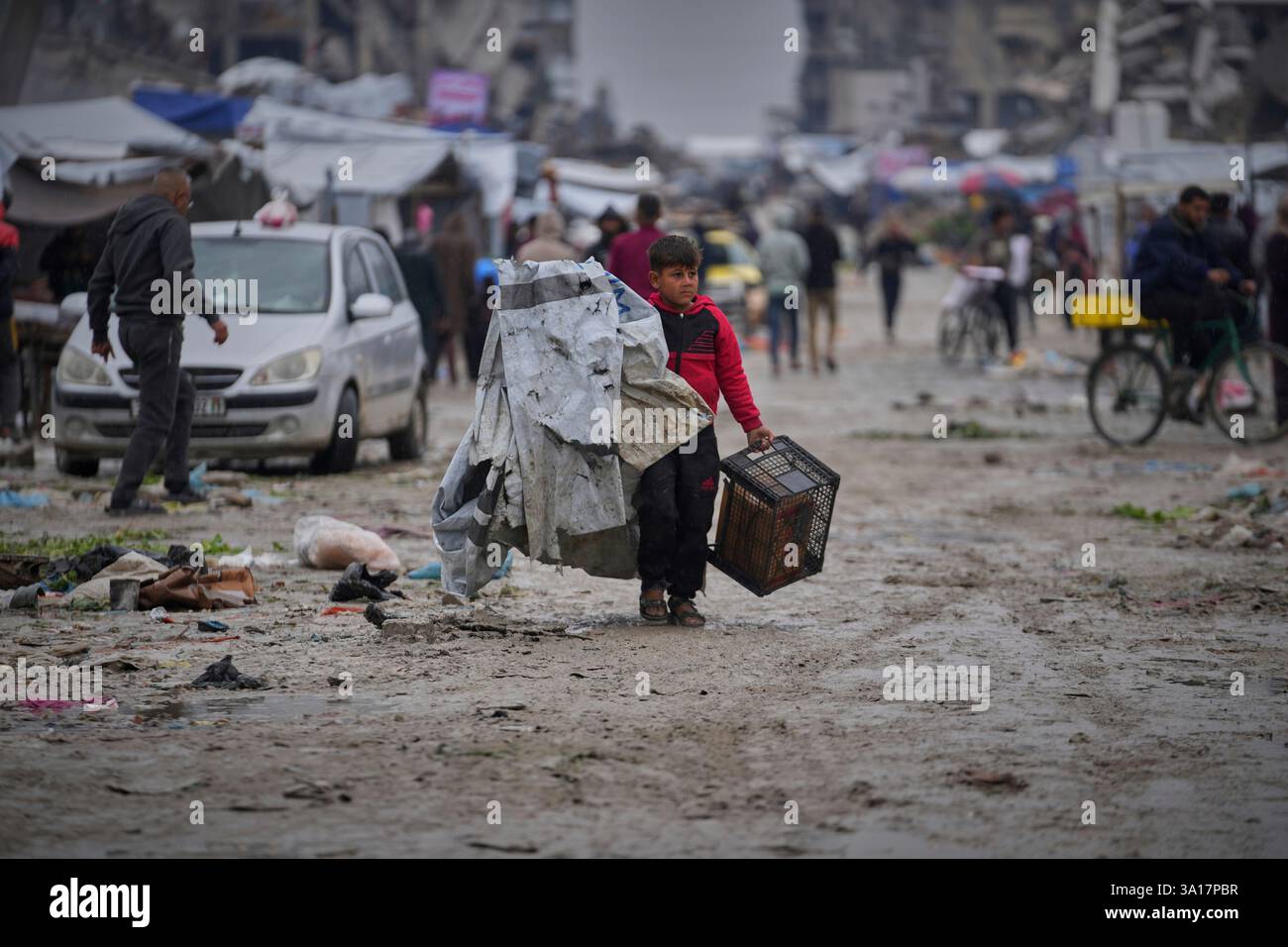 A boy carries fabric and a plastic box at a street market in Jabaliya ...