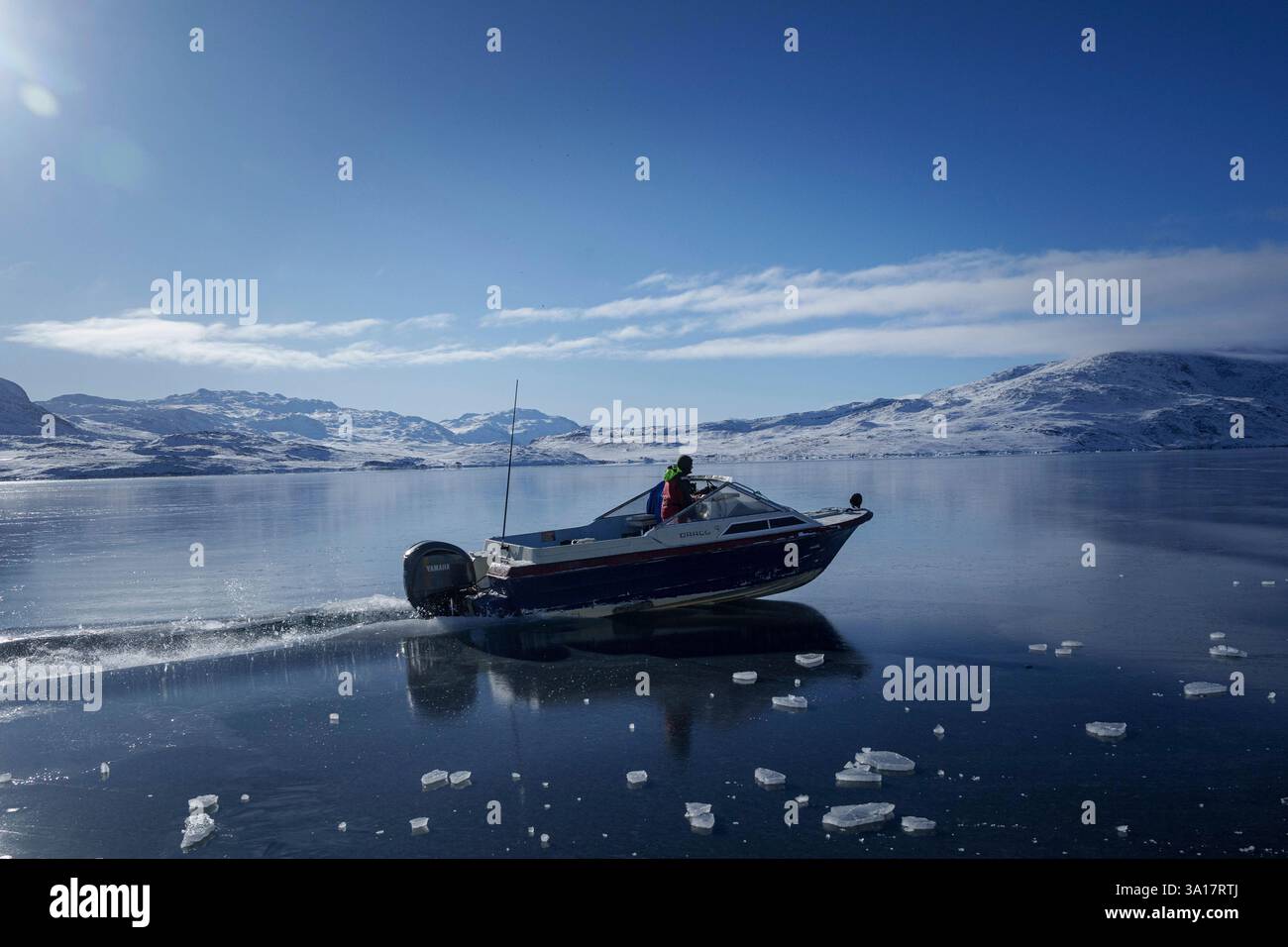 A fisherman rides on a boat though a frozen sea inlet outside of Nuuk ...