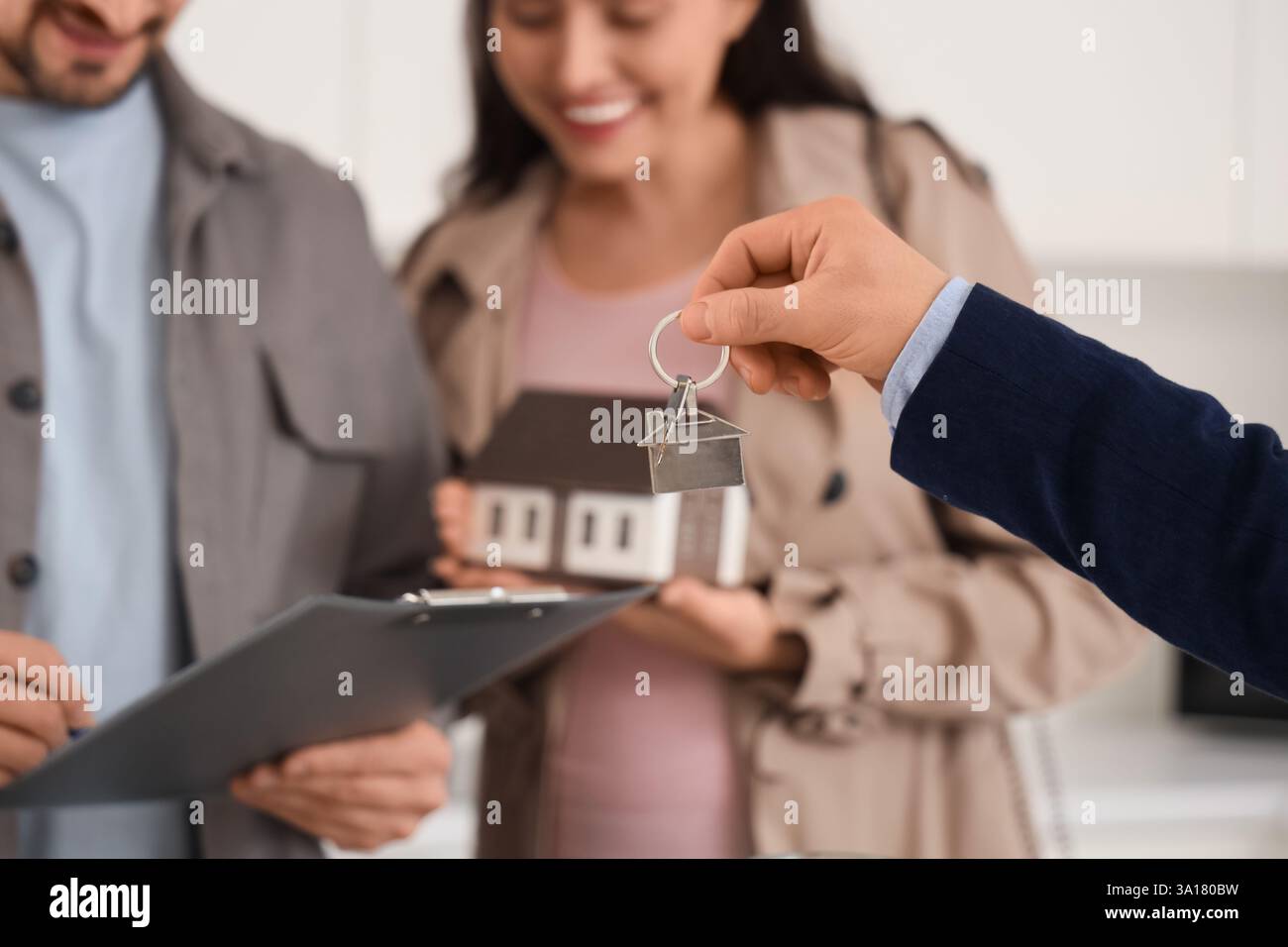 Male realtor with key against couple signing house rental agreement in ...