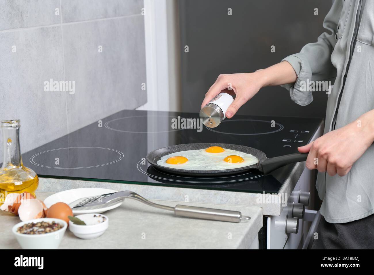 Woman adding salt into frying pan while cooking eggs on cooktop in ...