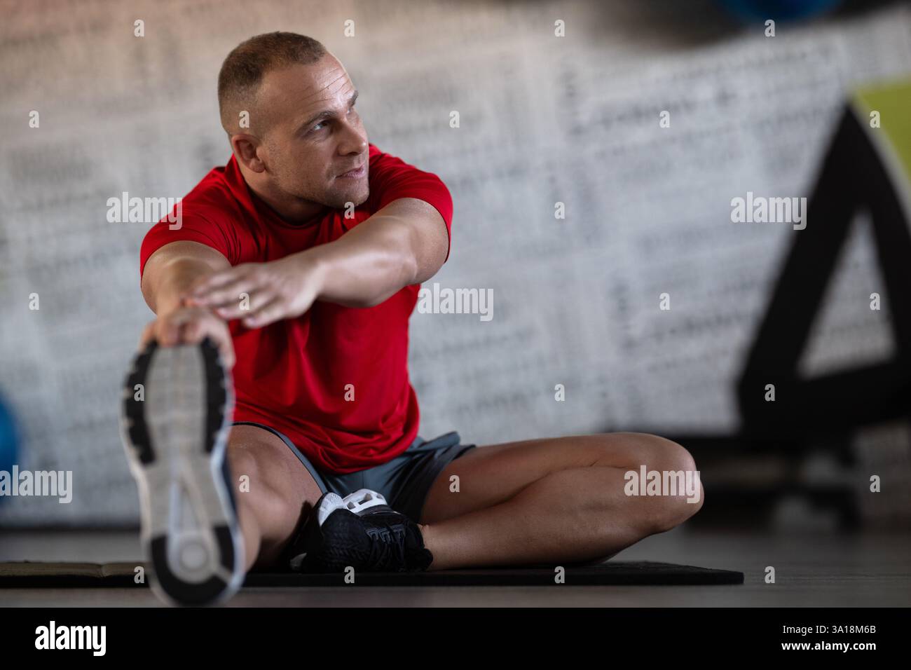 A fitness man stretches in the gym after an intense workout, focusing on recovery and ...