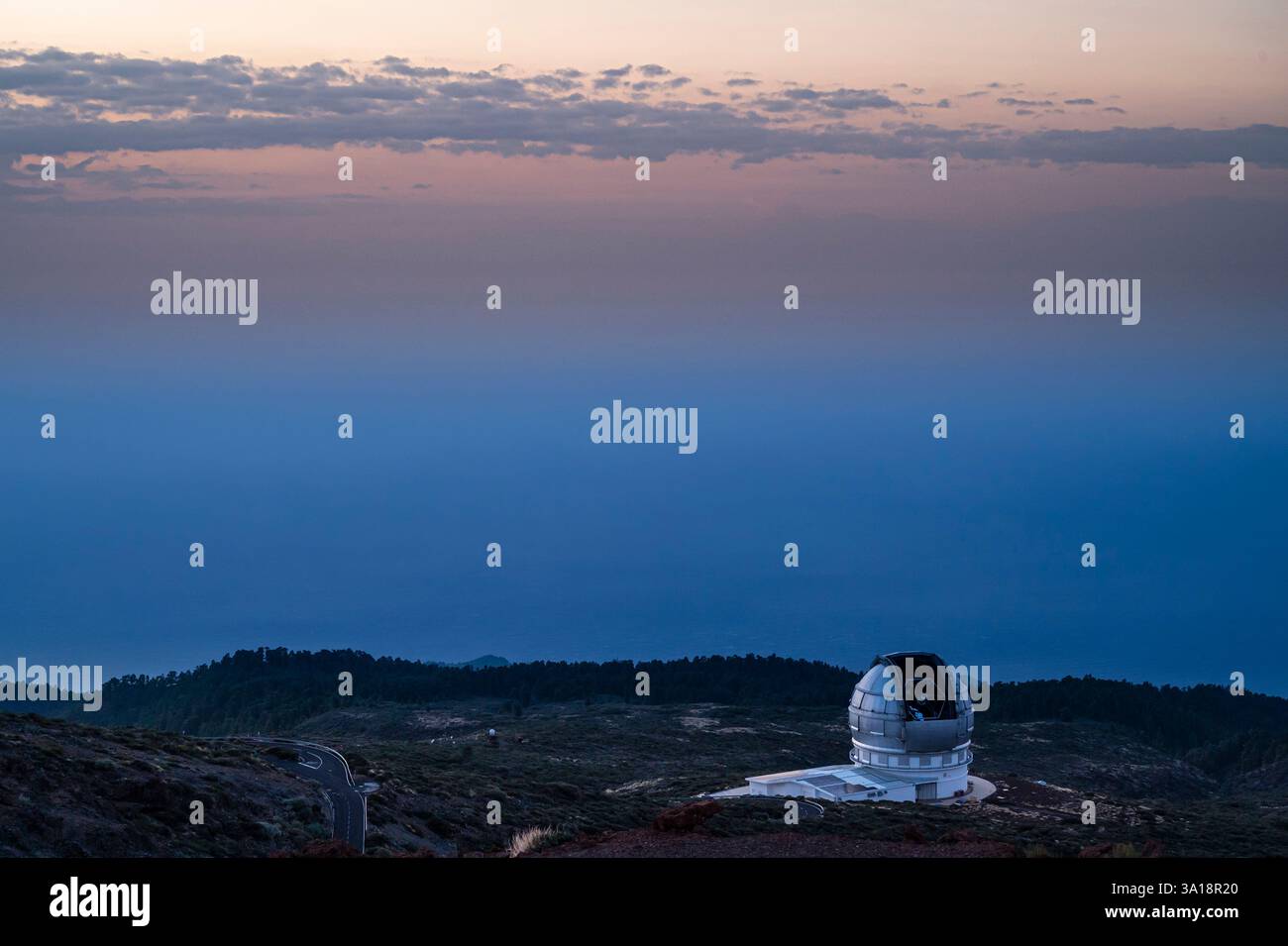 A large telescope with the hatch open, stands on a hill overlooking the ...