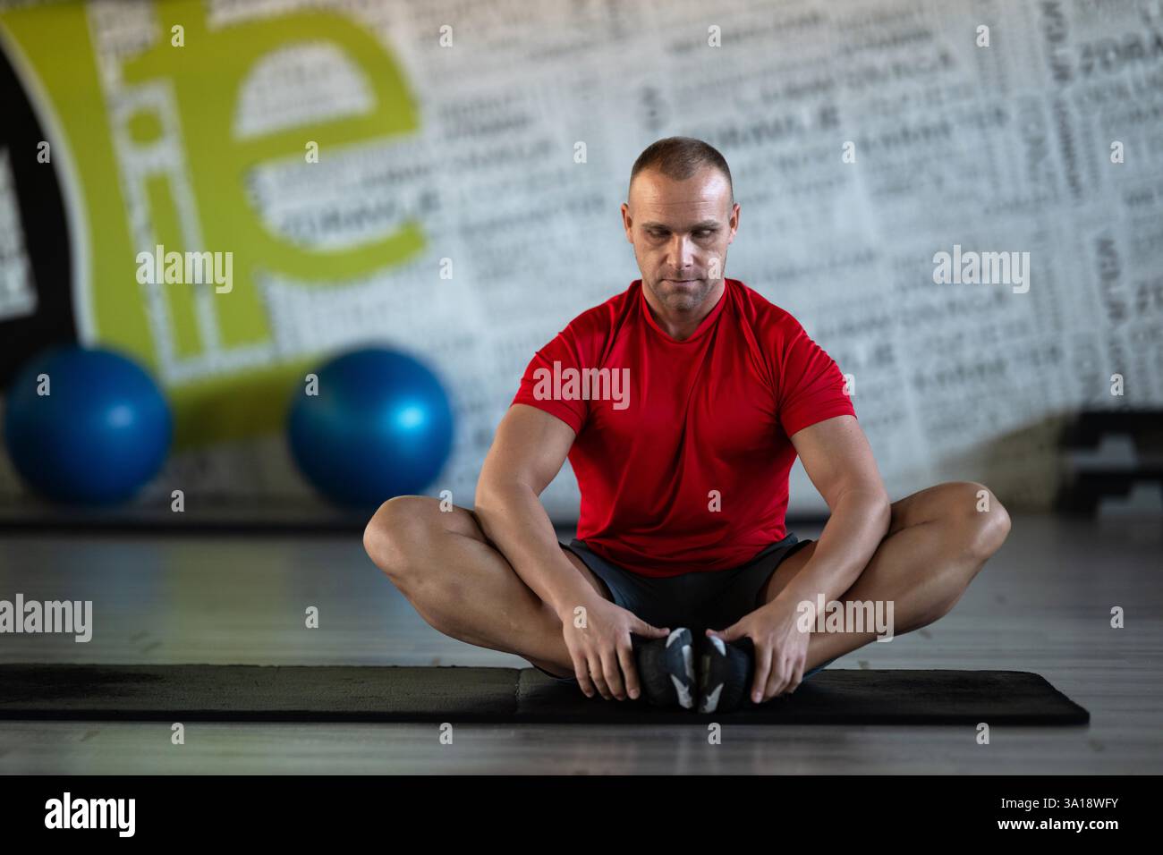 A fitness man stretches in the gym after an intense workout, focusing ...