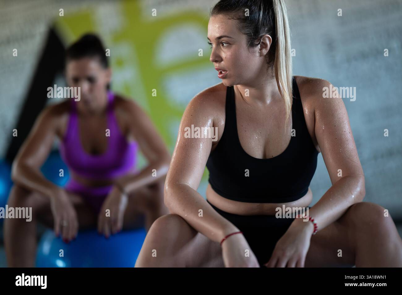 Two fitness women resting and recovering in the gym after an intense workout session, showcasing ...