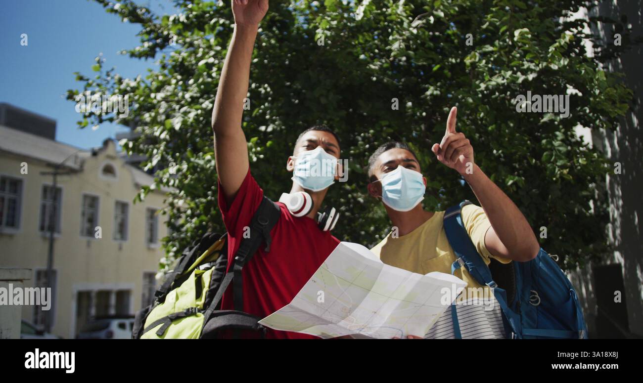 Two biracial male friends wearing face masks using map in the street ...