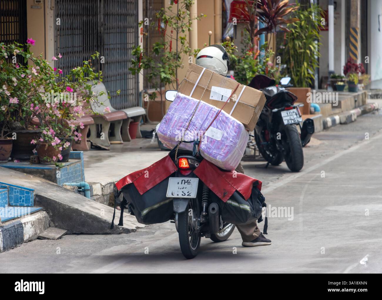 A postman with a motorbike loaded with parcels stands on the street ...