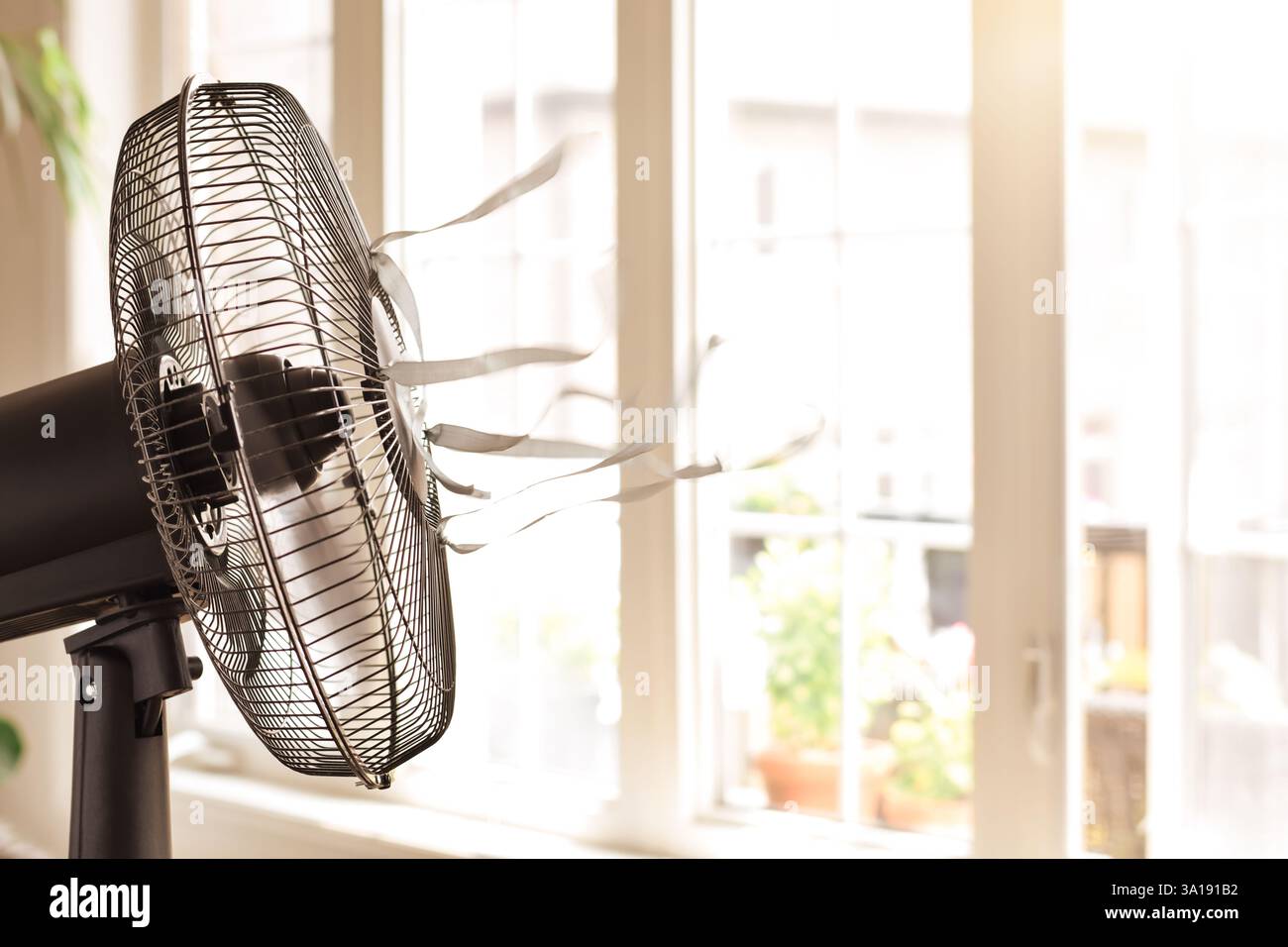 Closeup electric cooling fan with blowing ribbons in front of window on ...