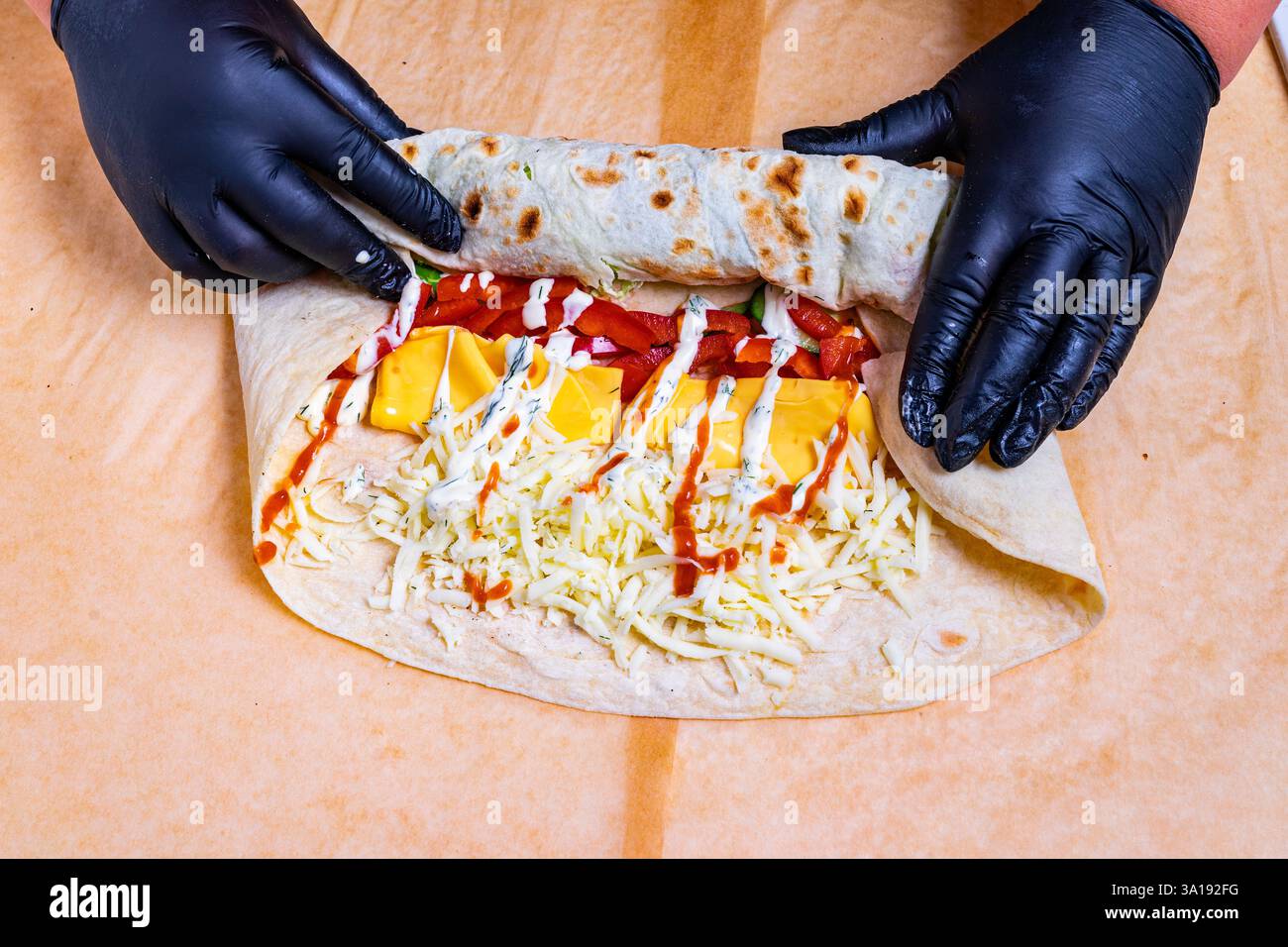 Hands in black gloves skillfully wrap a tortilla filled with cheese ...