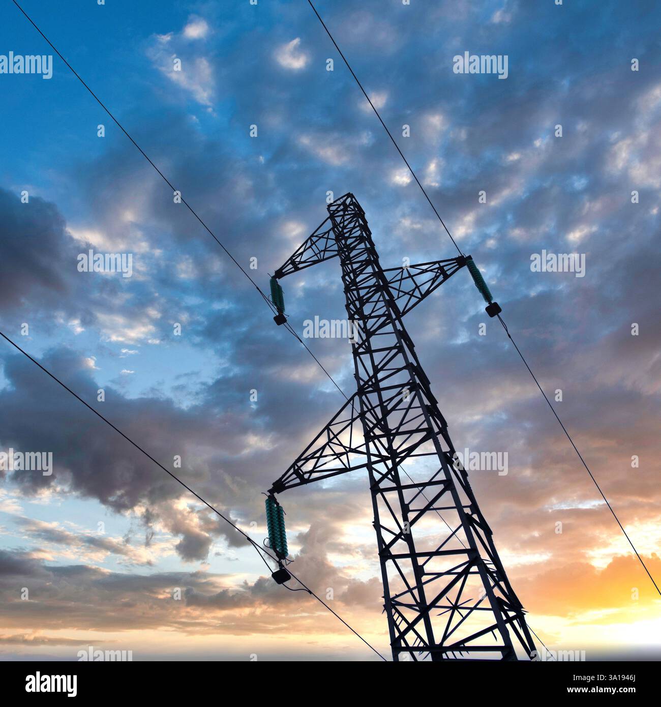 A tall transmission tower stands silhouetted against a vibrant sunset ...
