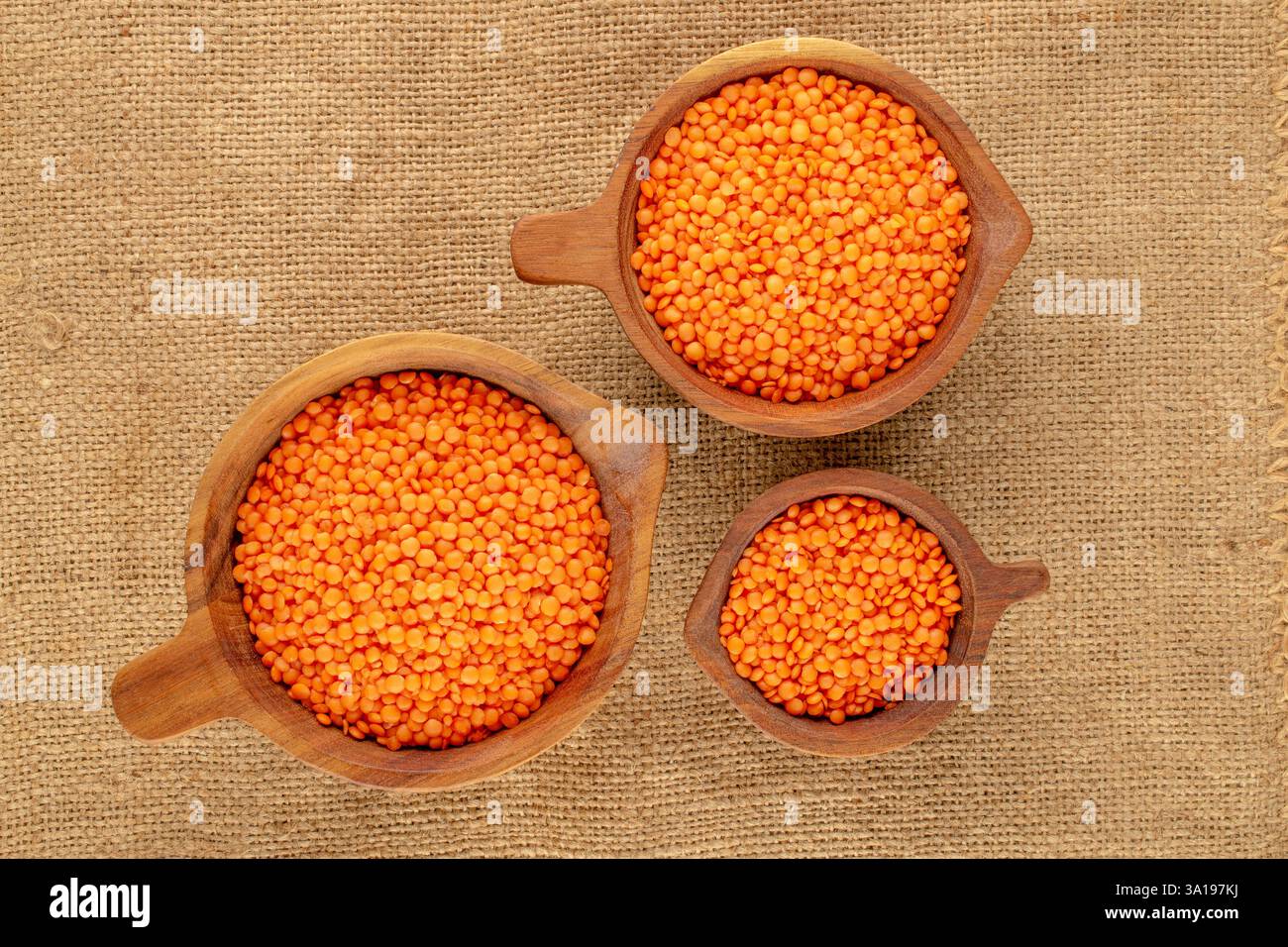 Red lentils in three wooden cups on jute cloth, close-up, top view ...