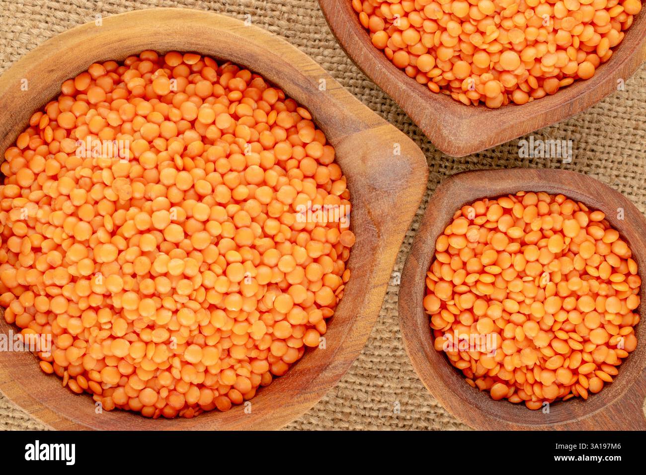 Red lentils in three wooden cups on jute cloth, close-up, top view ...