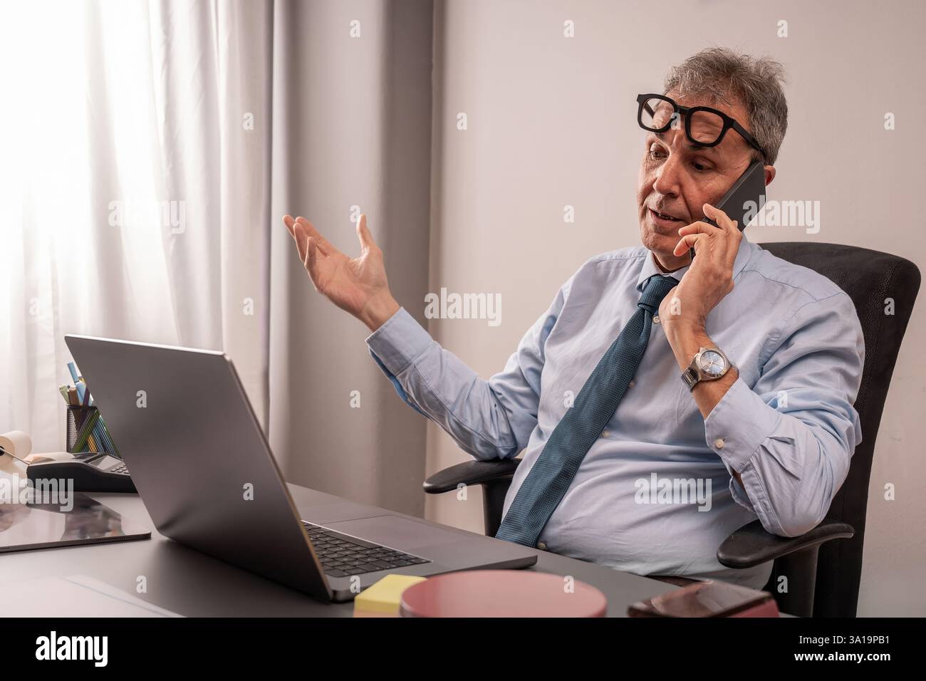 Senior businessman at office desk engaged in a phone conversation ...