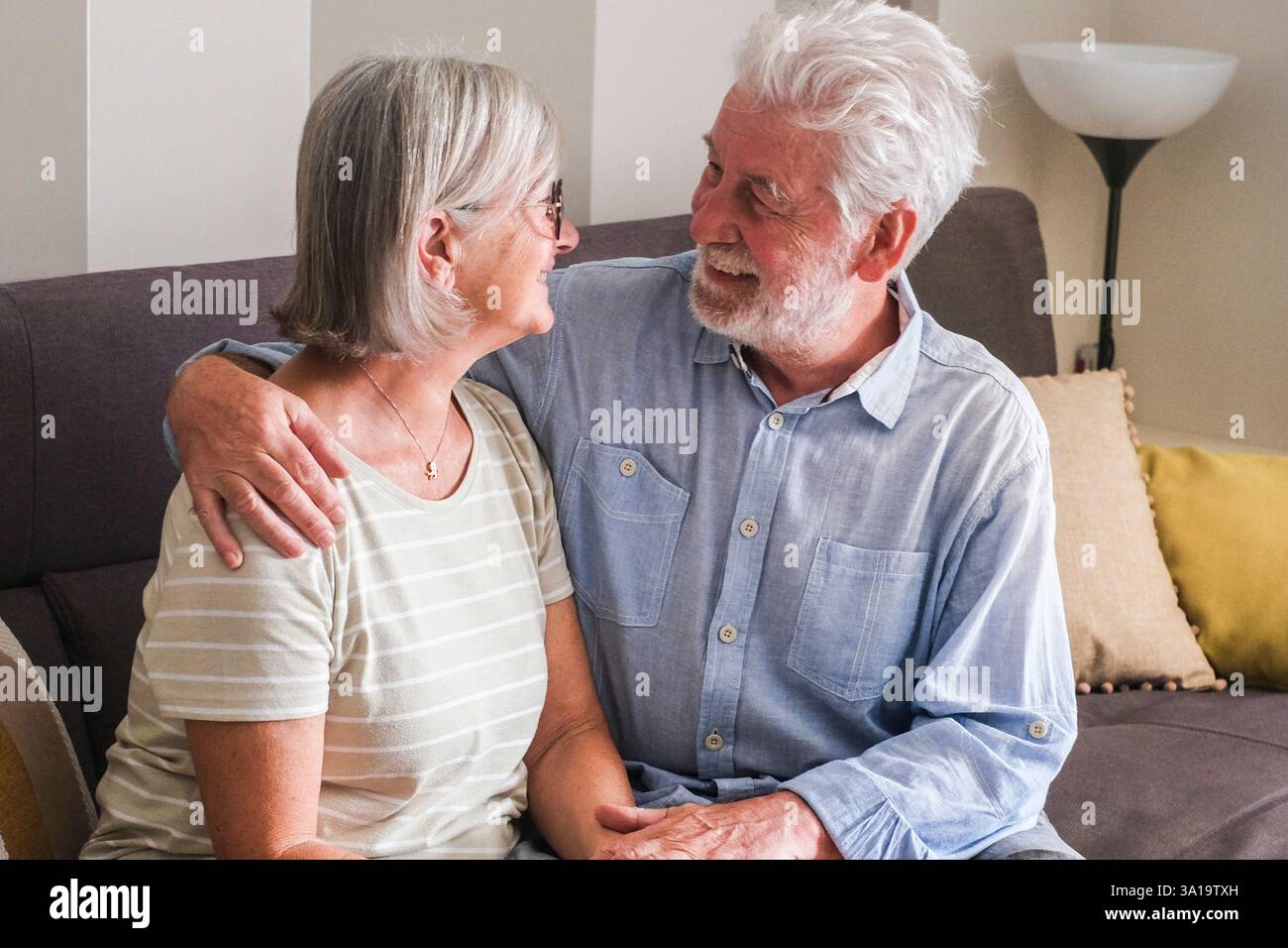 Elderly couple sitting together on a cozy couch at home, smiling and enjoying the warmth of a ...
