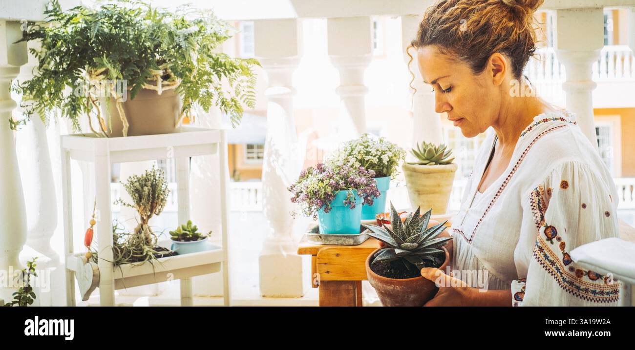 Beautiful lady takes care of her plants on the balcony. Sitting blonde ...