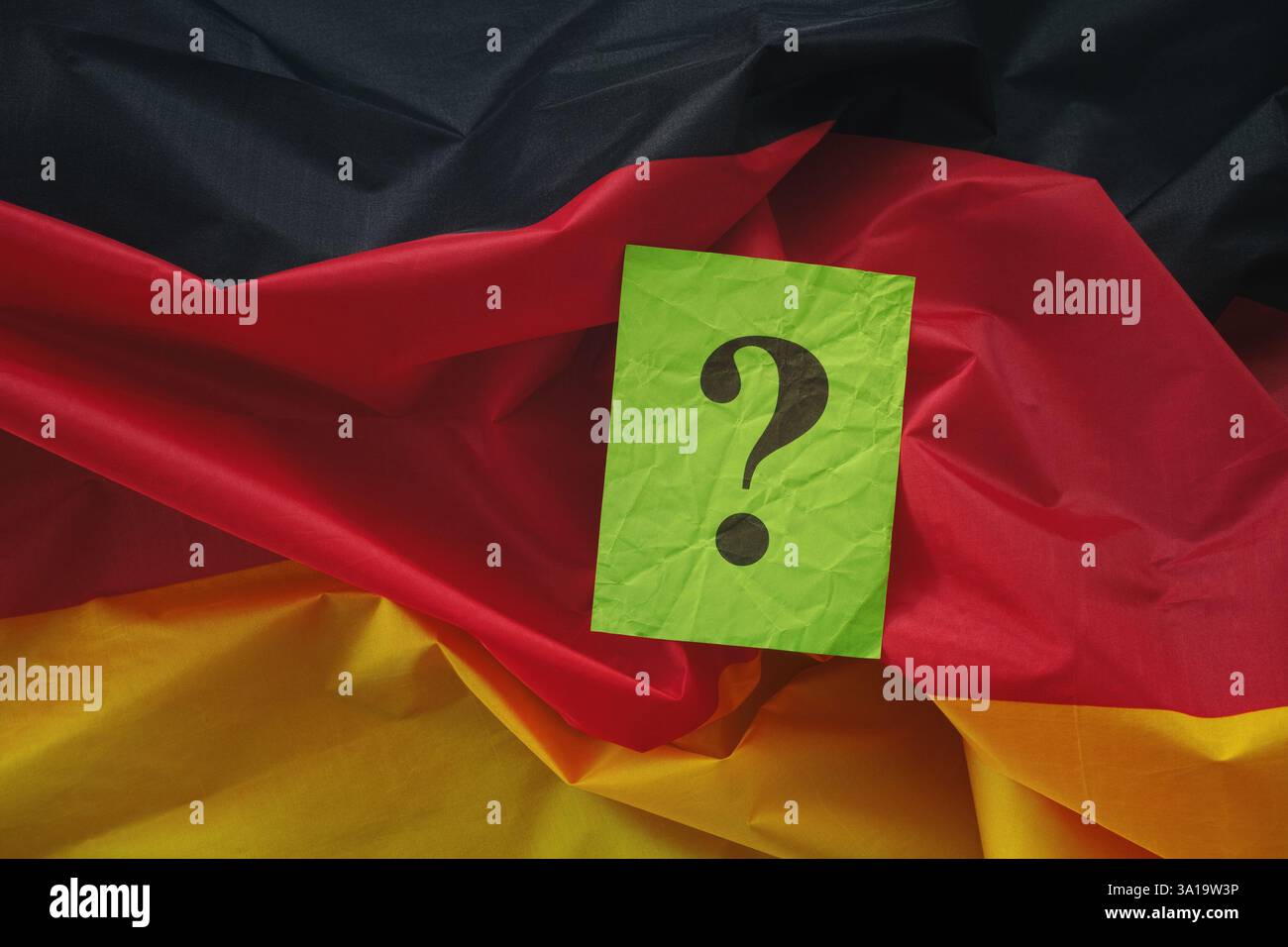 A green paper note with a question mark on it lying on the German flag ...