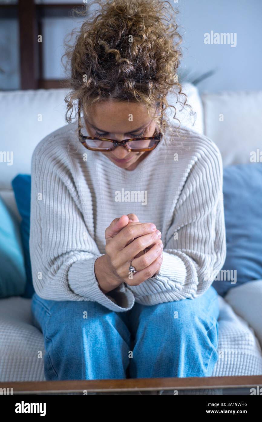 Upset and sad adult woman sitting on sofa with clasped hands looking ...