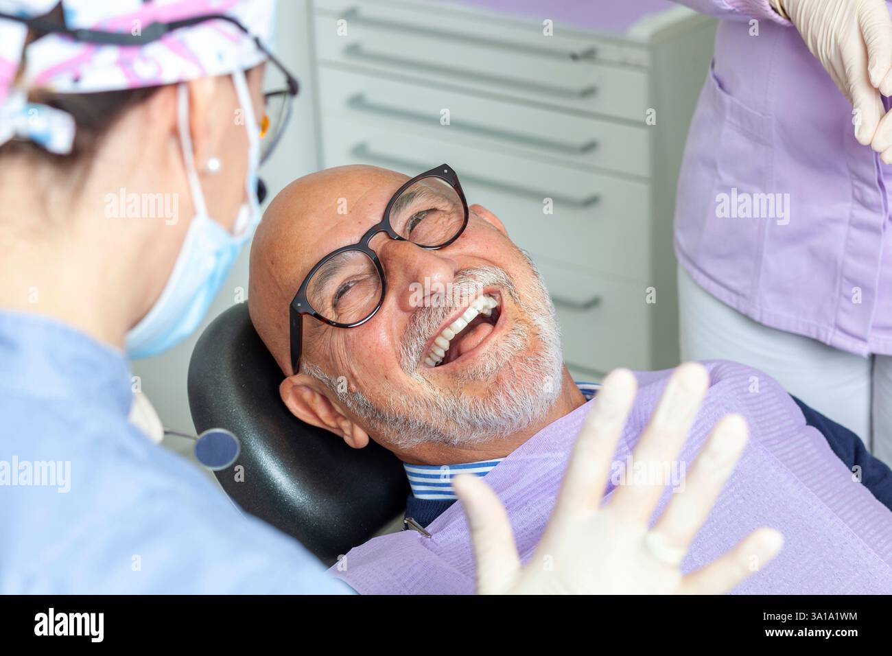 Happy senior man laughing during his dental checkup at the clinic, showing his healthy teeth ...