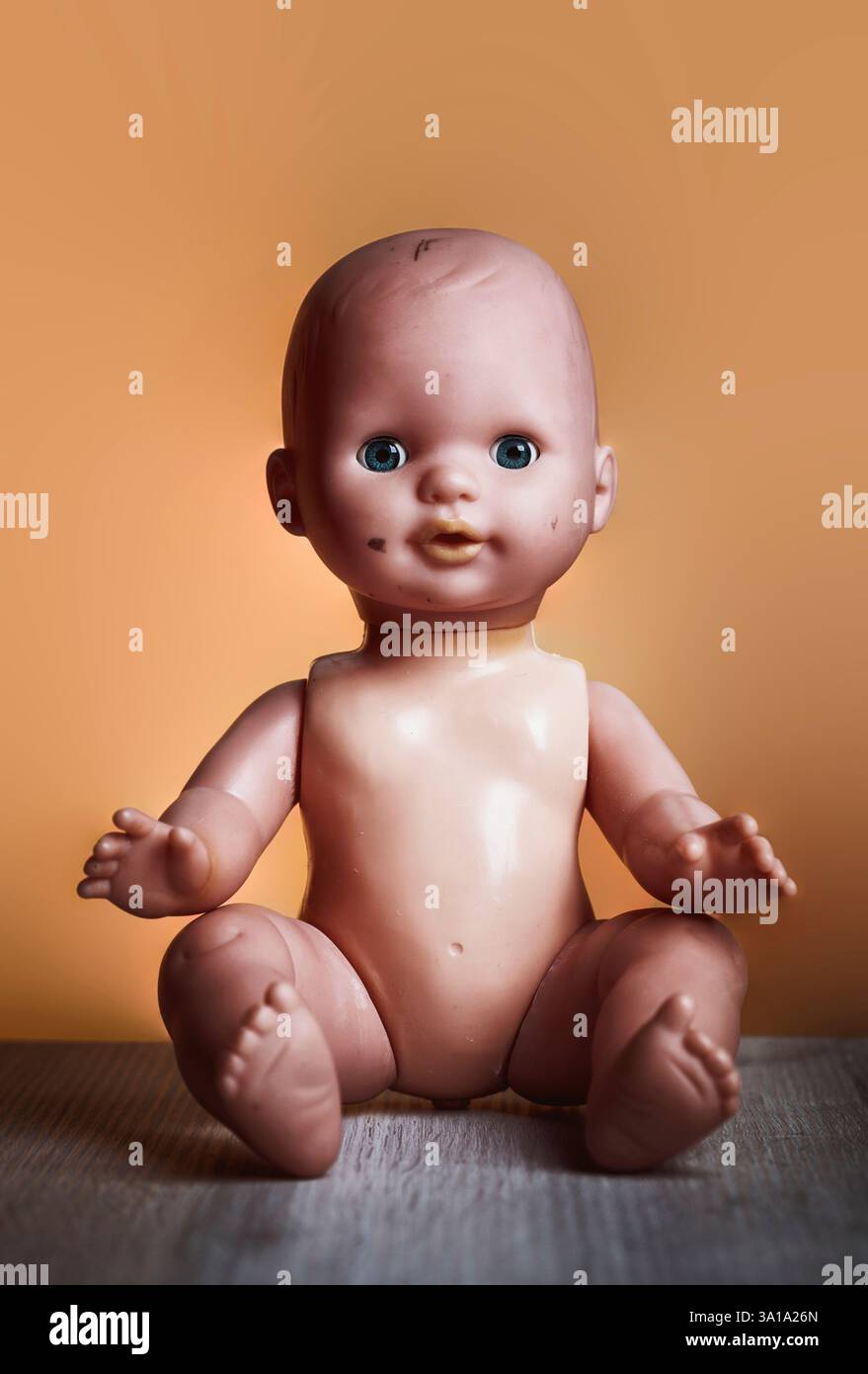 Old used plastic baby doll is sitting on a table against a yellow ...
