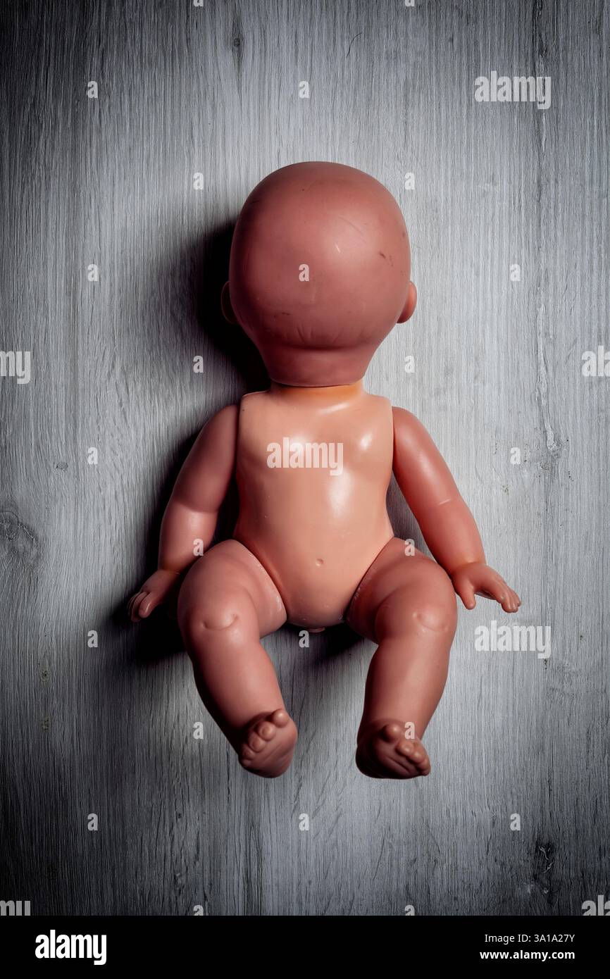 Old plastic baby doll sits on a wooden background, looking slightly ...