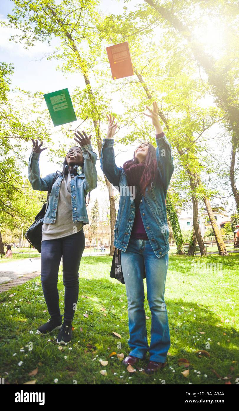 Two female students, one Caucasian and the other African, throw books ...