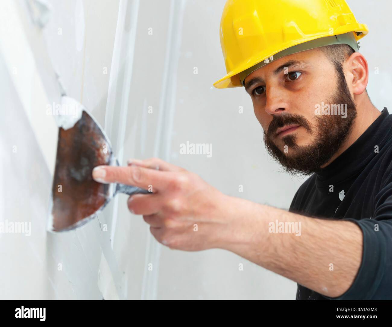 Construction worker wearing a safety helmet plastering a white wall ...